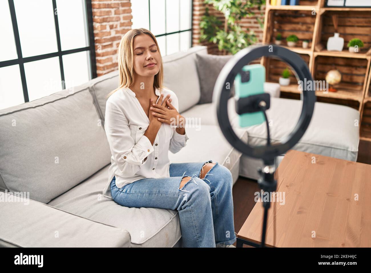 Young blonde woman recording vlog tutorial with smartphone at home ...