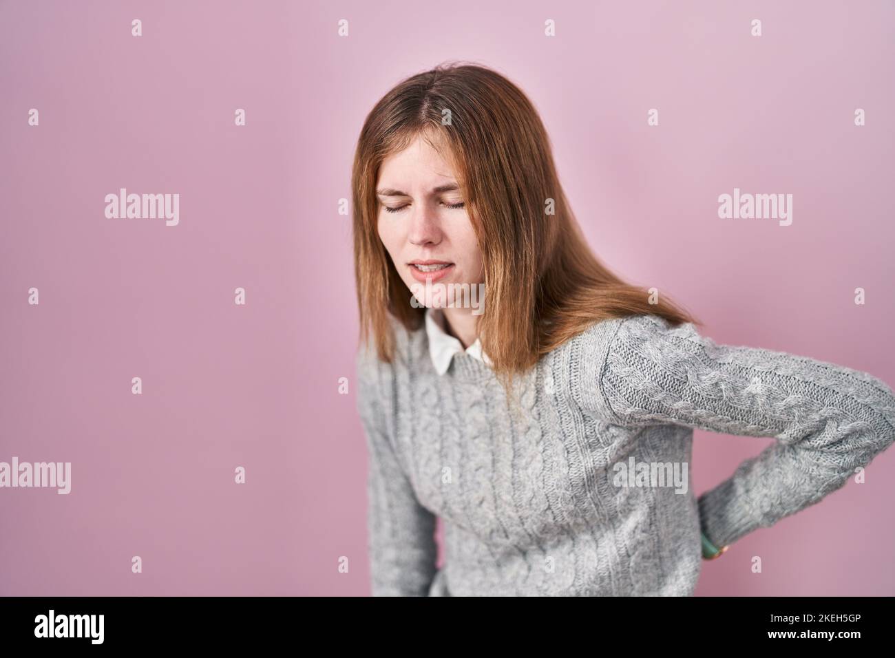 Beautiful woman standing over pink background suffering of backache ...
