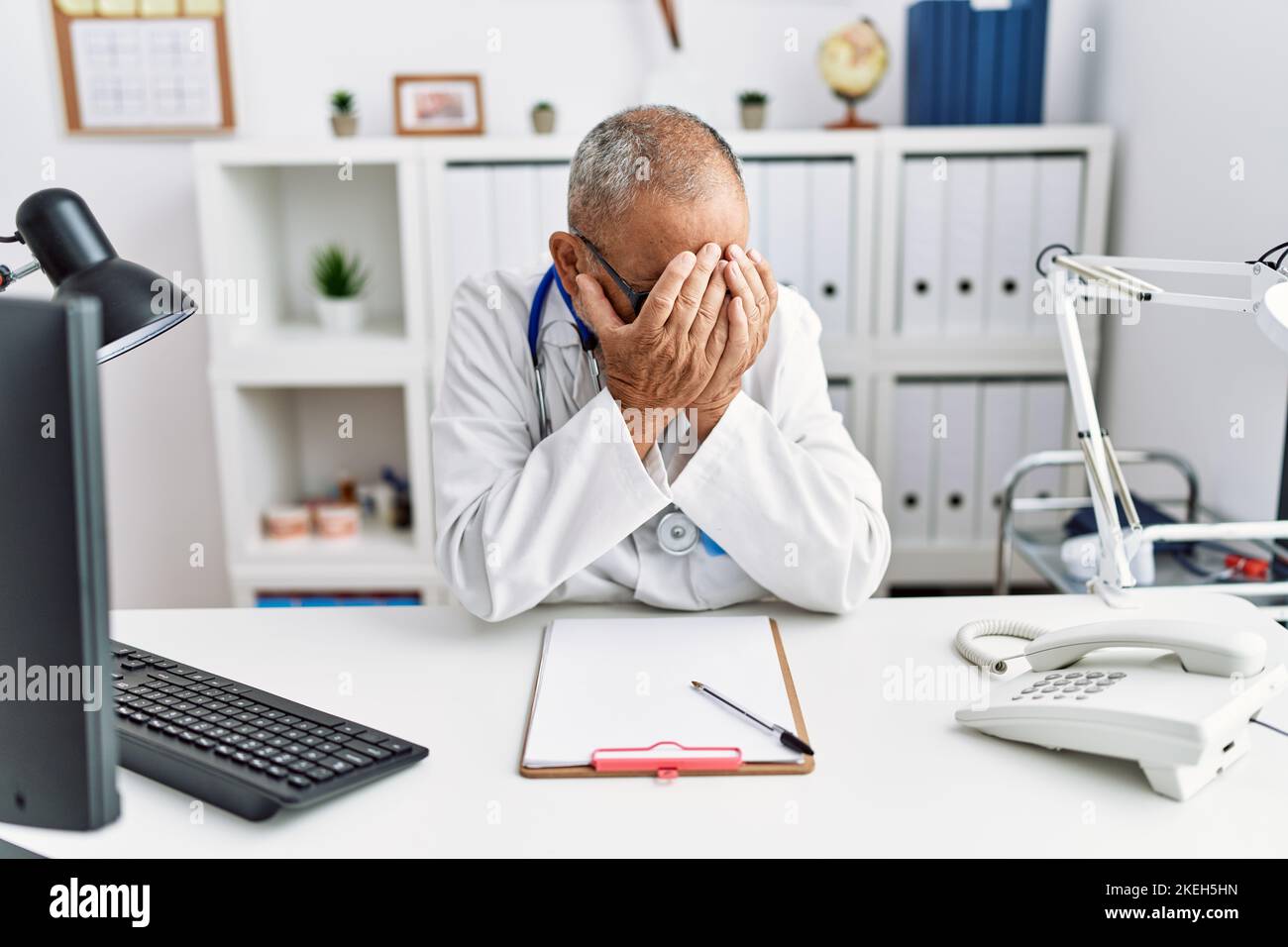 Mature doctor man at the clinic with sad expression covering face with ...