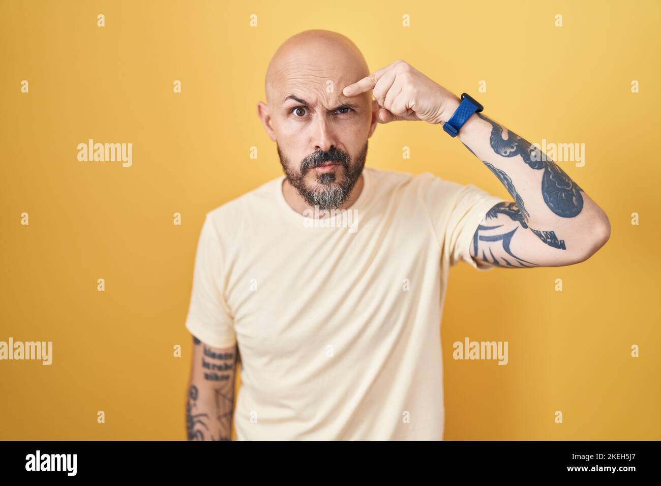 Hispanic man with tattoos standing over yellow background pointing ...