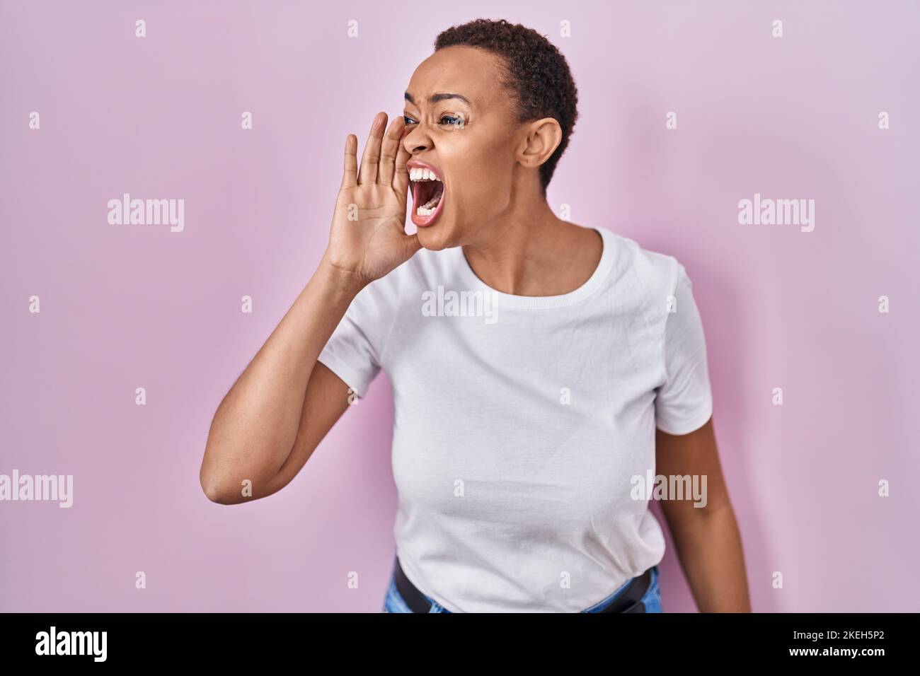 Beautiful african american woman standing over pink background shouting ...