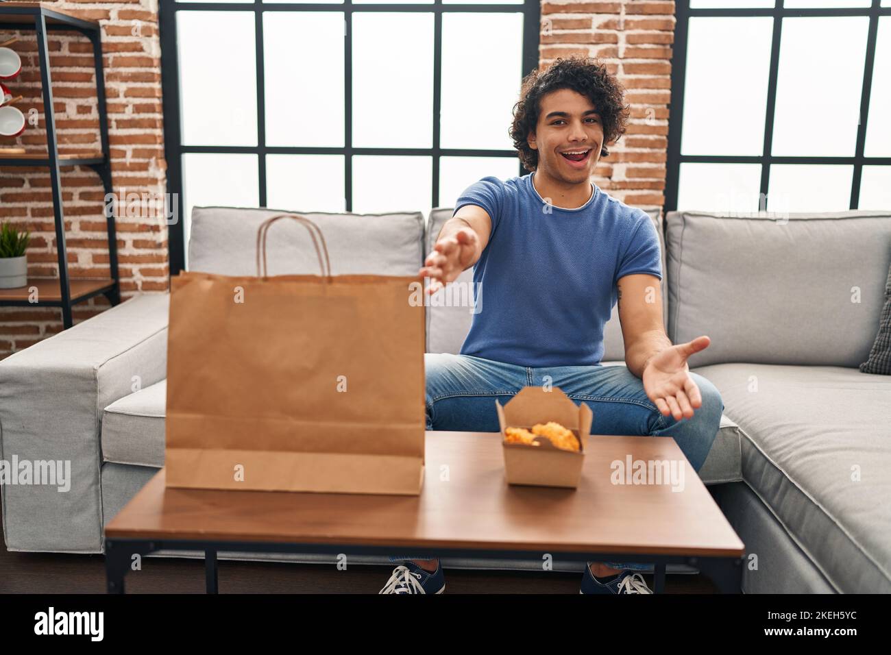 Hispanic man with curly hair eating chicken wings looking at the camera ...