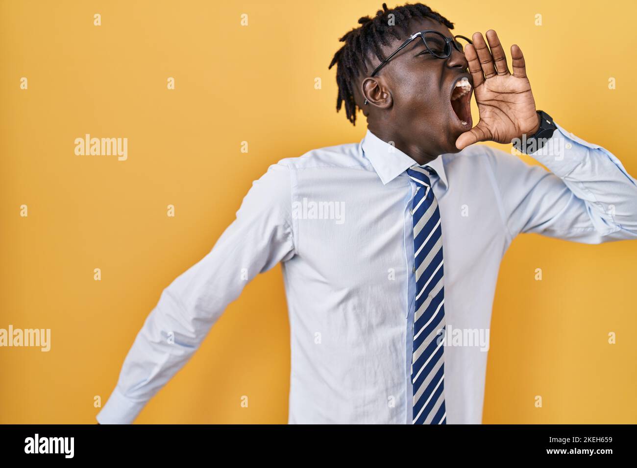 African man with dreadlocks standing over yellow background shouting ...