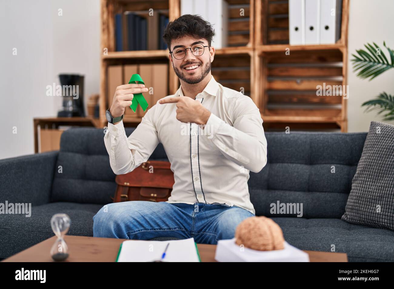 Hispanic man with beard holding support green ribbon at therapy clinic ...