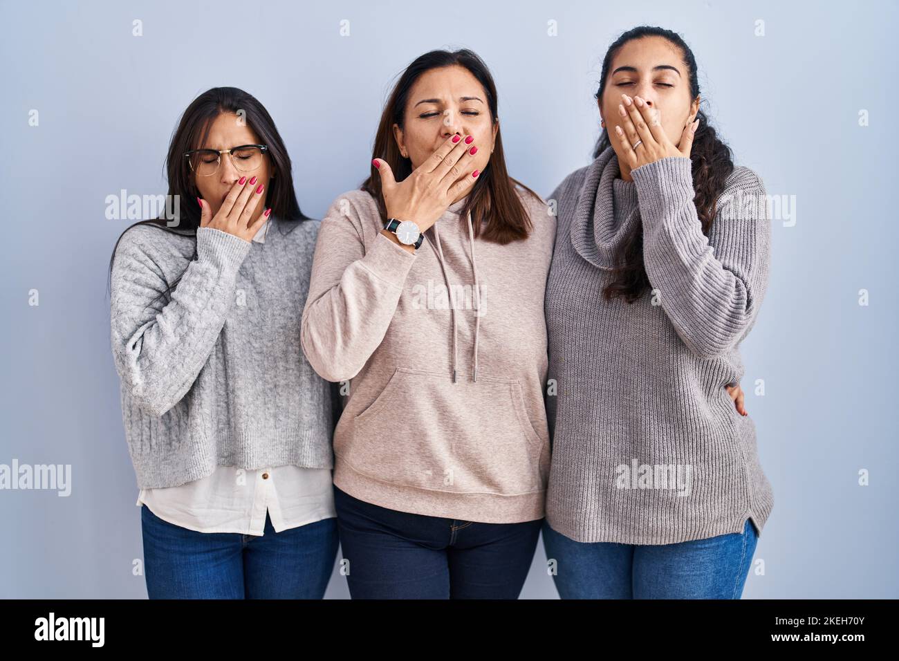 Mother and two daughters standing over blue background bored yawning ...