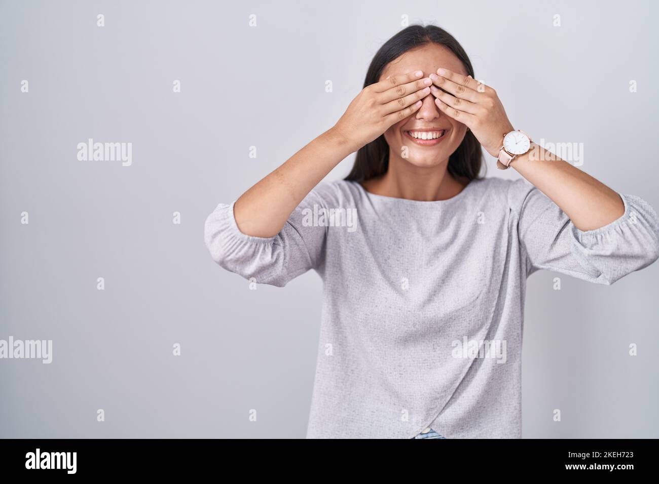 Young hispanic woman standing over white background covering eyes with ...