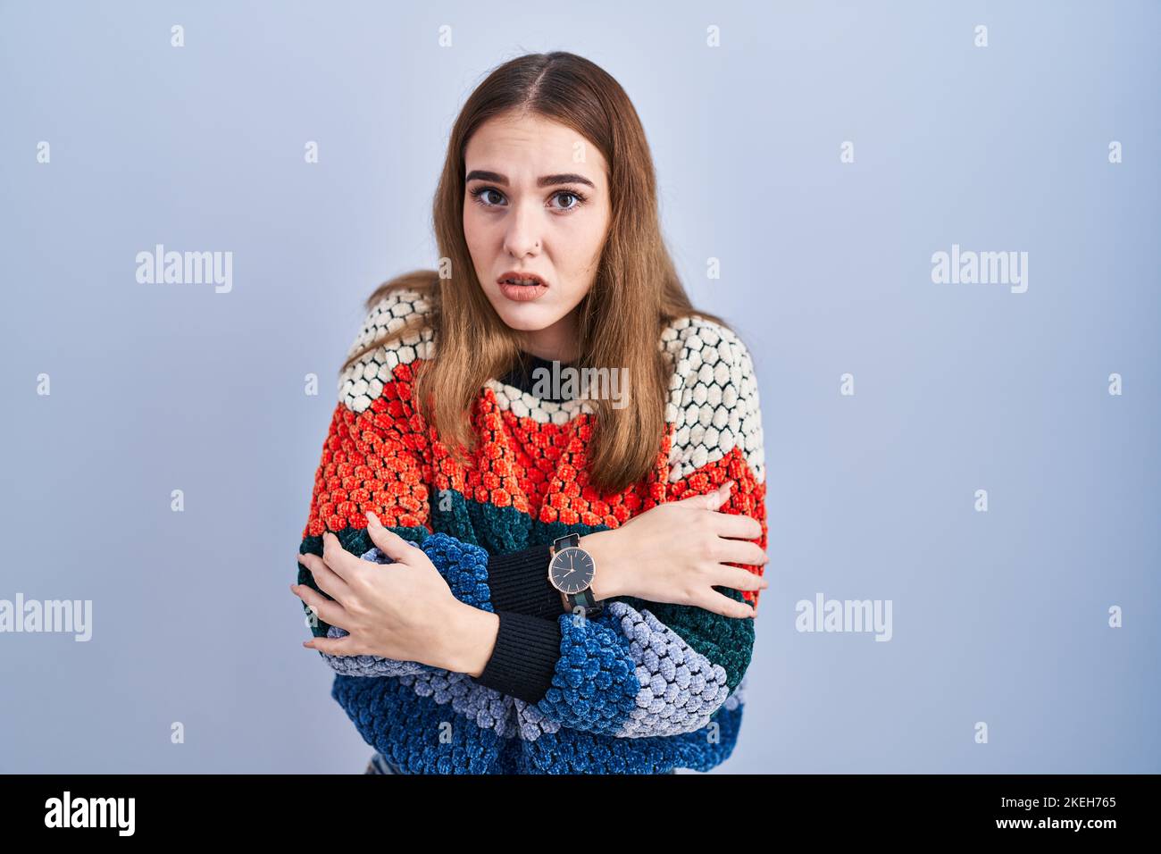 Young hispanic girl standing over blue background shaking and freezing ...