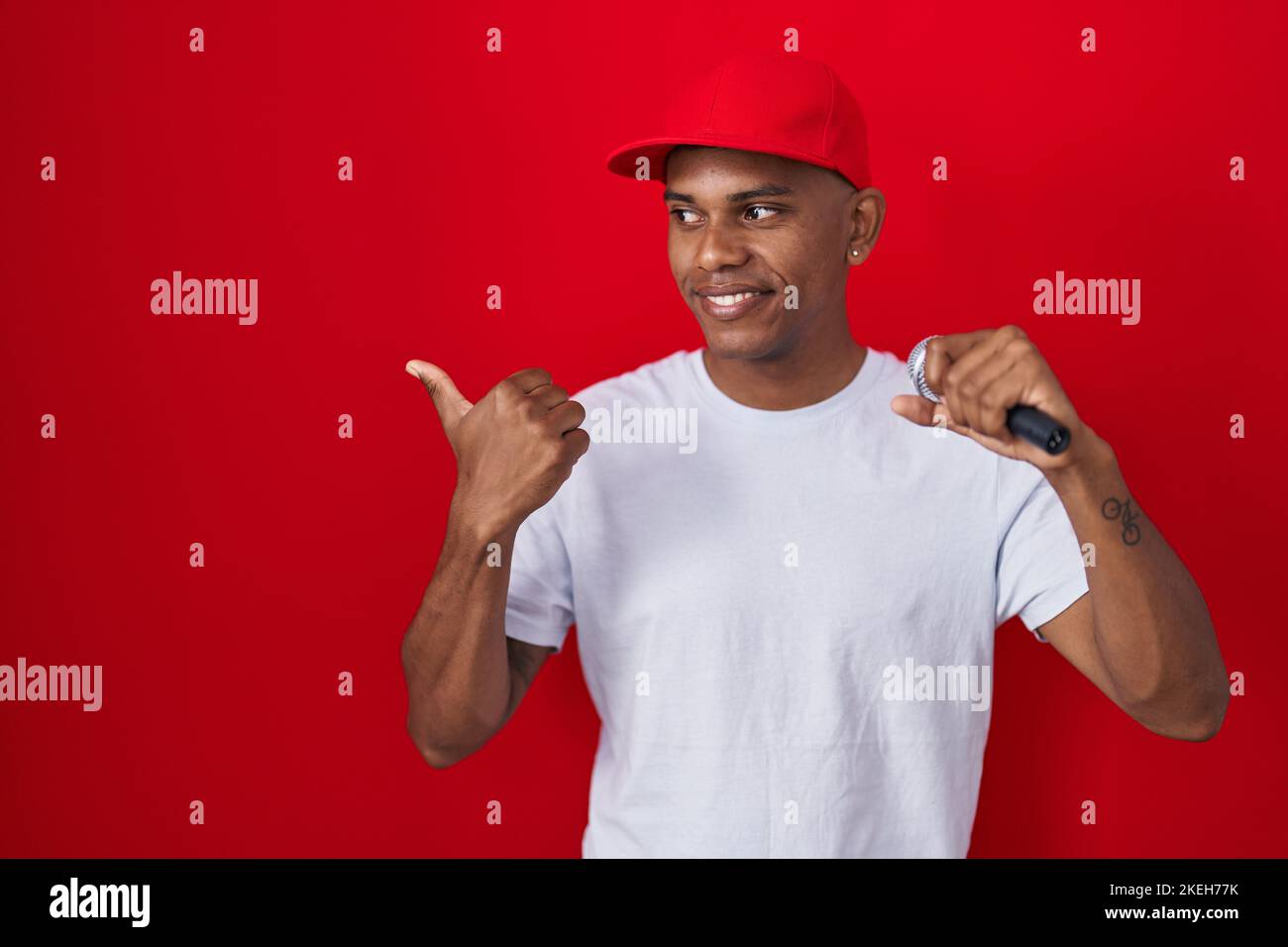 Young hispanic man singing song using microphone pointing thumb up to ...