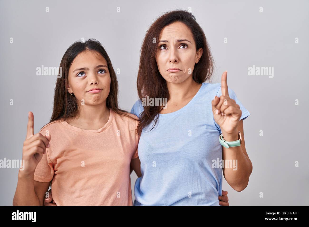 Young mother and daughter standing over white background pointing up ...