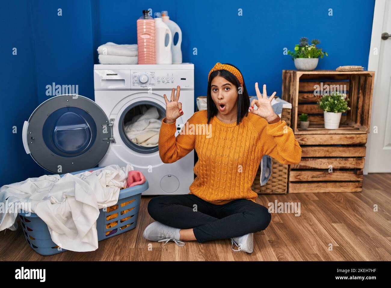 Young hispanic woman doing laundry looking surprised and shocked doing ...
