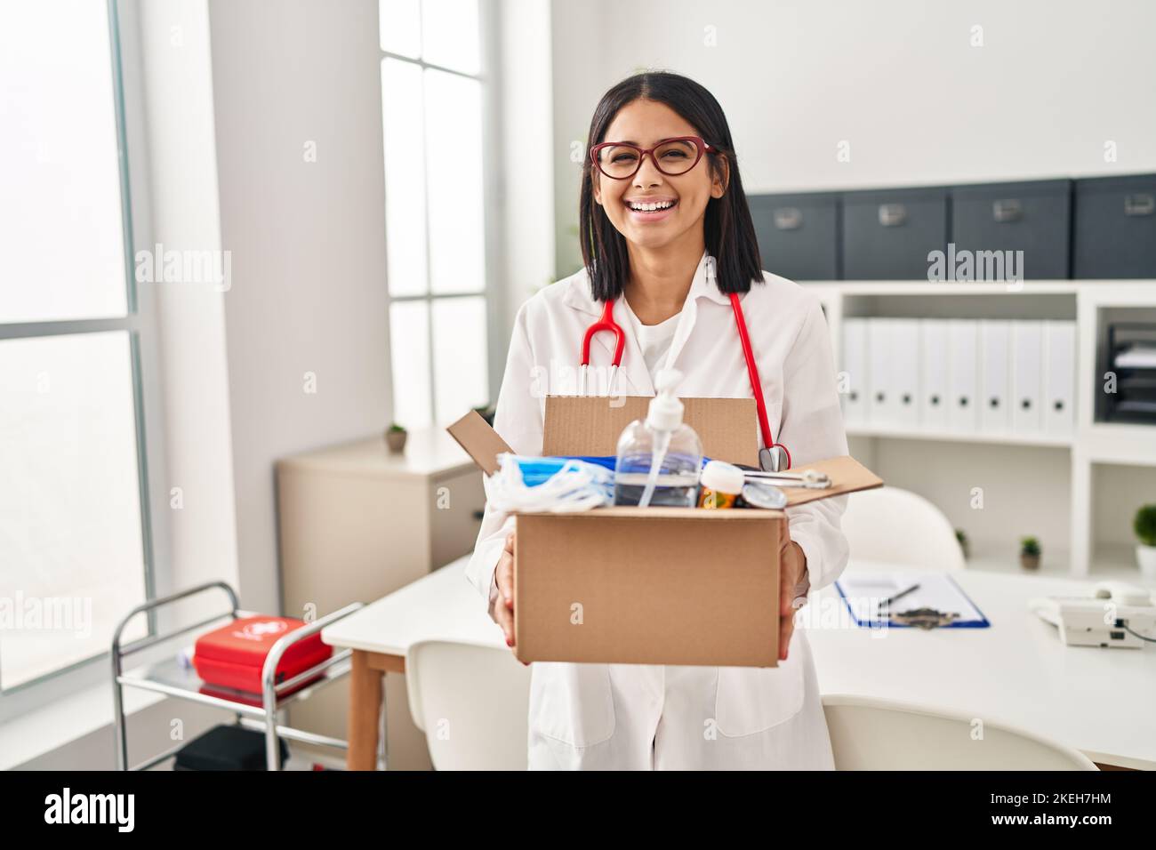 Young hispanic doctor woman holding box with medical items smiling and ...