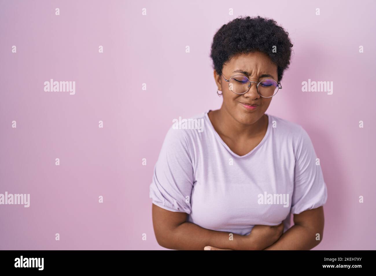 Young african american woman standing over pink background with hand on ...
