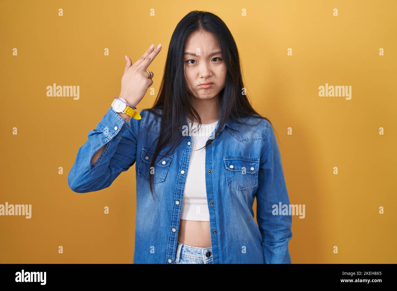 Young asian woman standing over yellow background shooting and killing ...