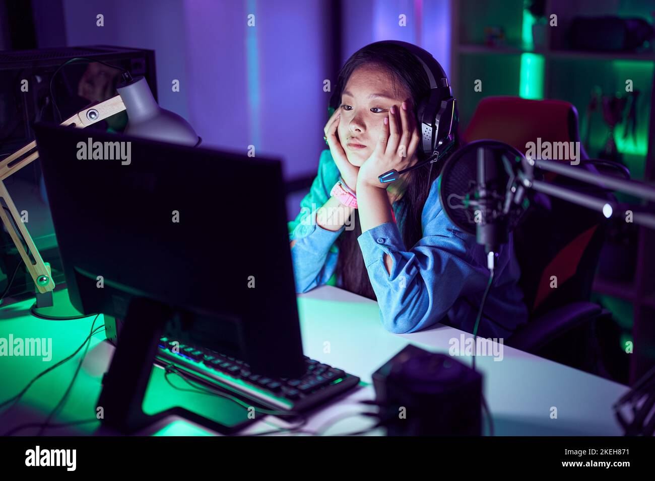 Young chinese woman streamer stressed using computer at gaming room ...