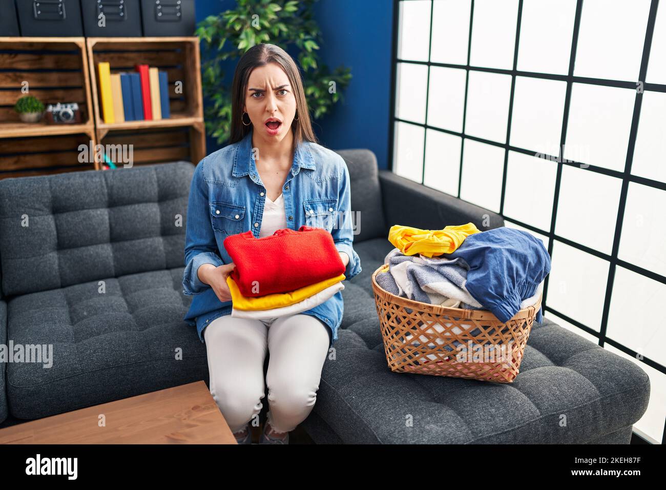 Hispanic woman holding folded laundry after ironing in shock face ...