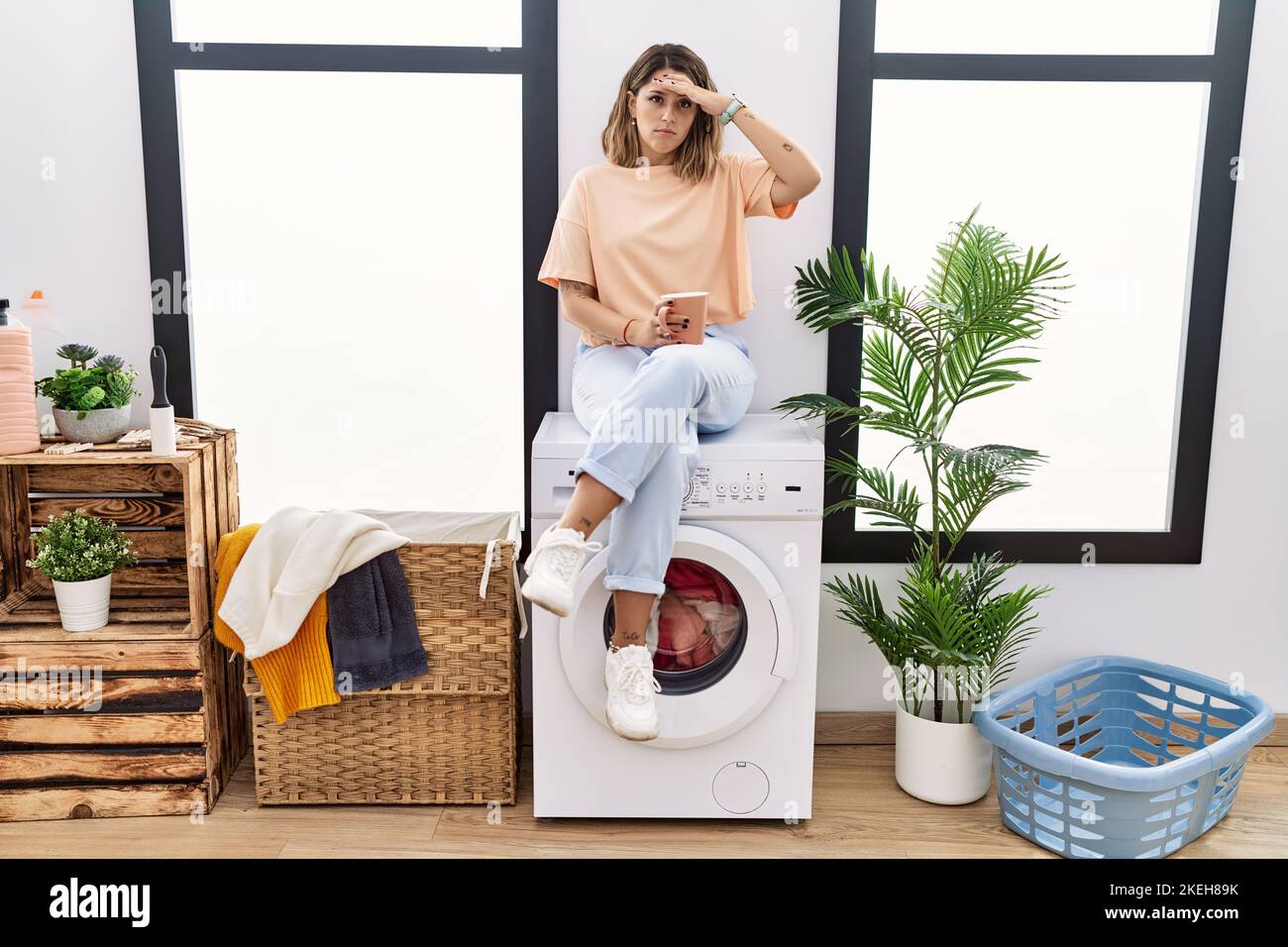 Young hispanic woman drinking coffee waiting for washing machine at ...