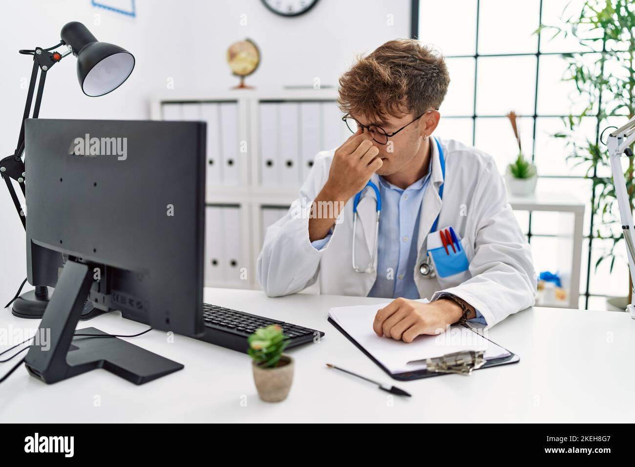 Young caucasian doctor man working at the clinic tired rubbing nose and ...