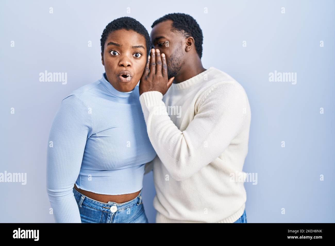 Young african american couple standing over blue background hand on ...