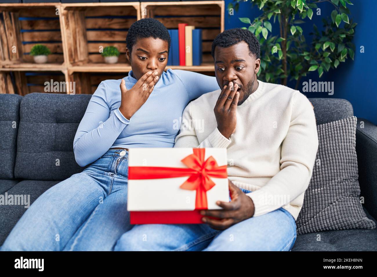 Young african american couple holding present covering mouth with hand ...