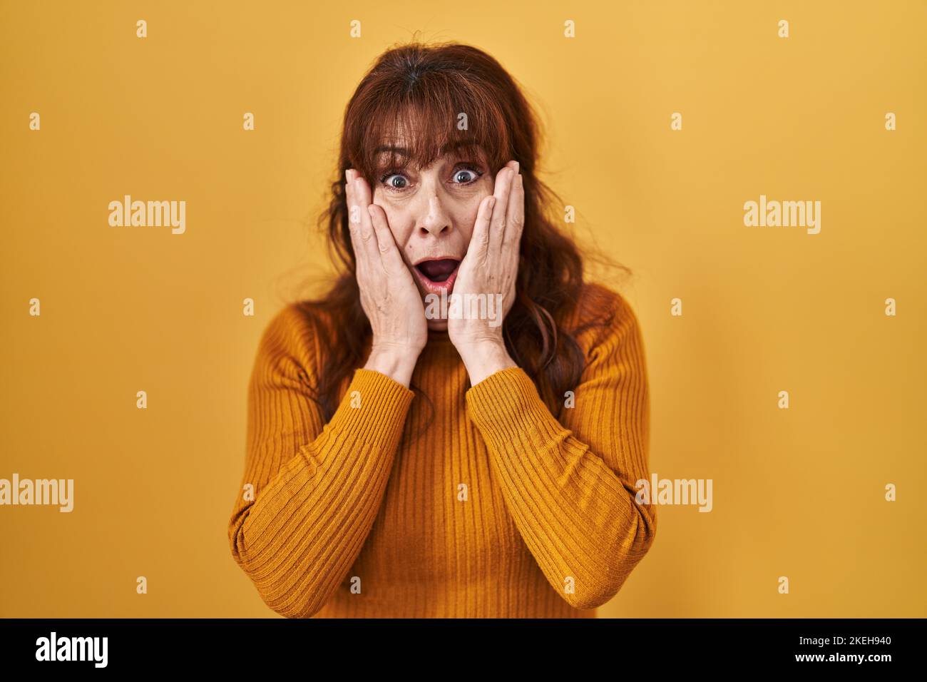 Middle age hispanic woman standing over yellow background afraid and ...