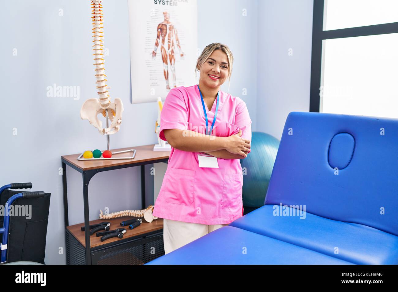 Young hispanic woman wearing physiotherapist uniform standing with arms ...