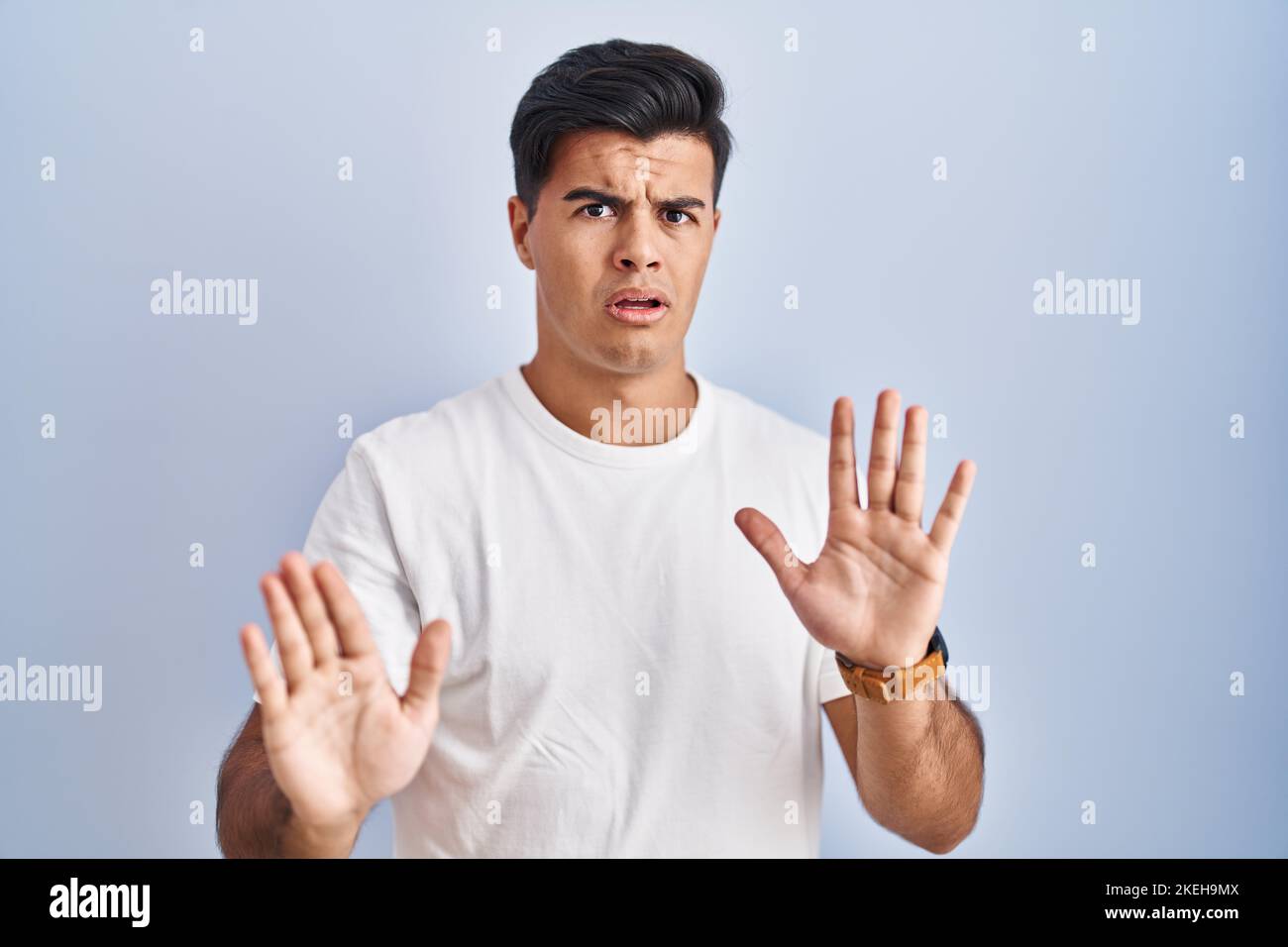 Hispanic man standing over blue background moving away hands palms ...