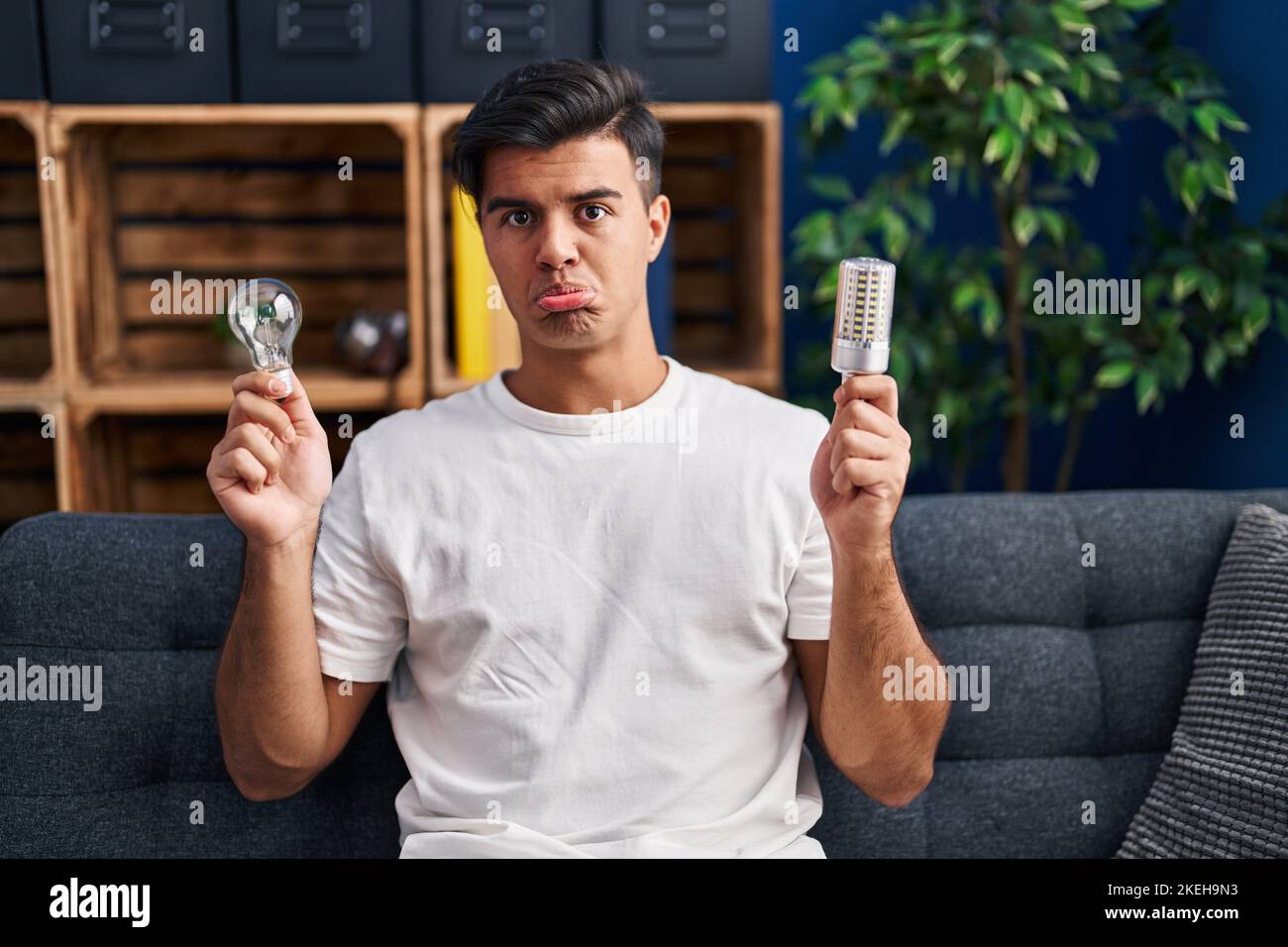 Hispanic man holding led lightbulb and incandescent bulb depressed and ...