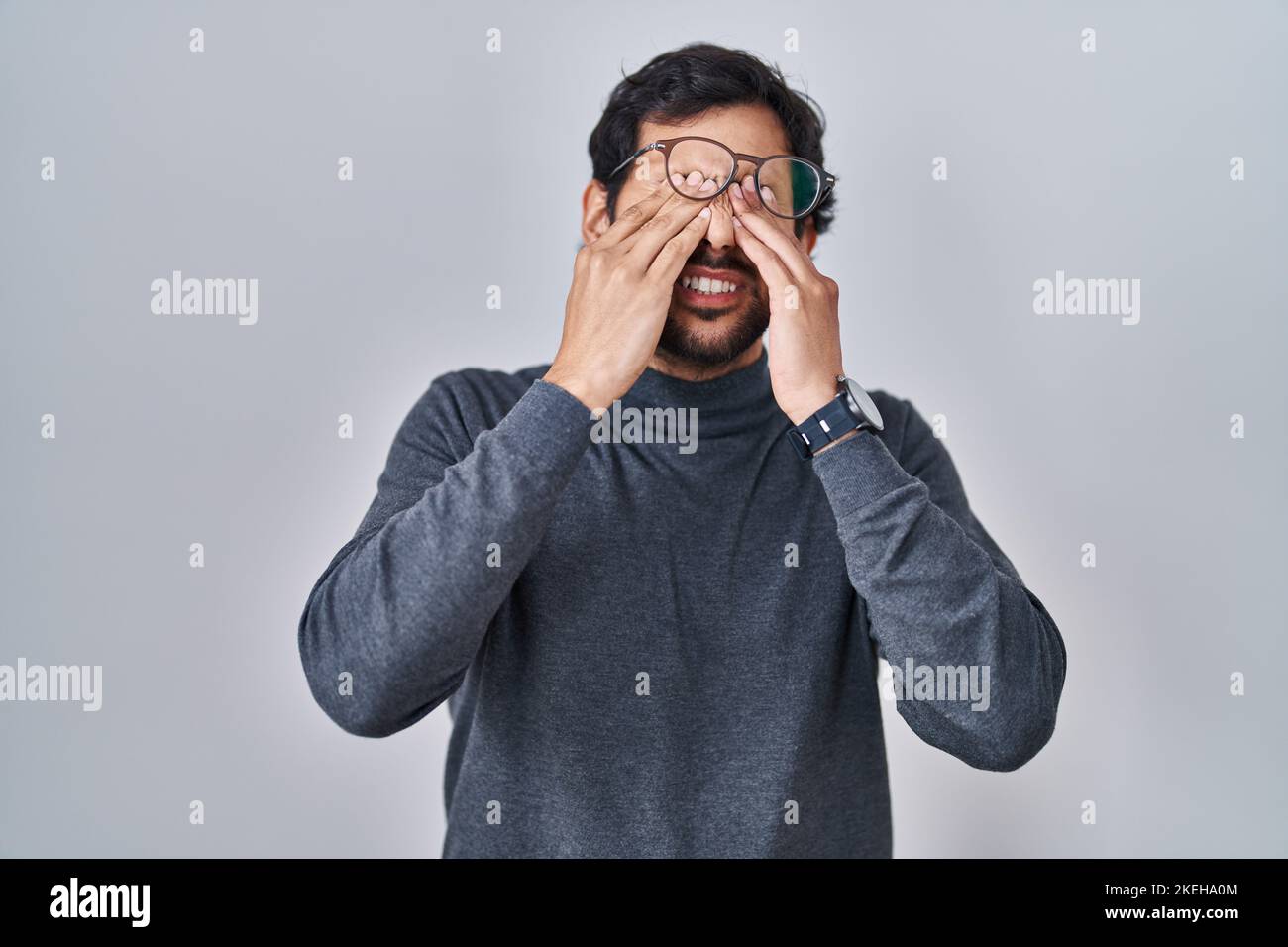 Handsome latin man standing over isolated background rubbing eyes for ...