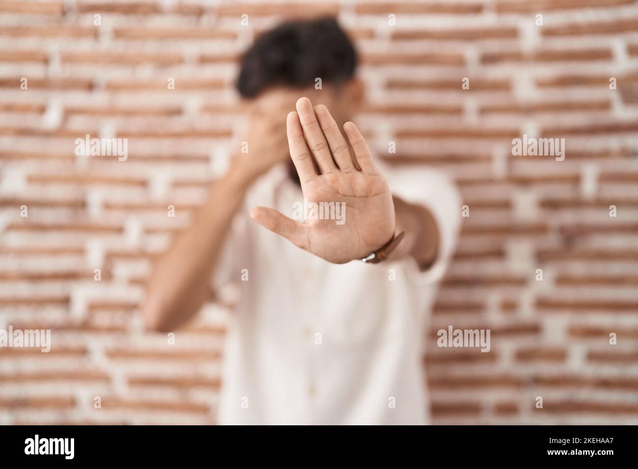 Arab man with beard standing over bricks wall background covering eyes ...