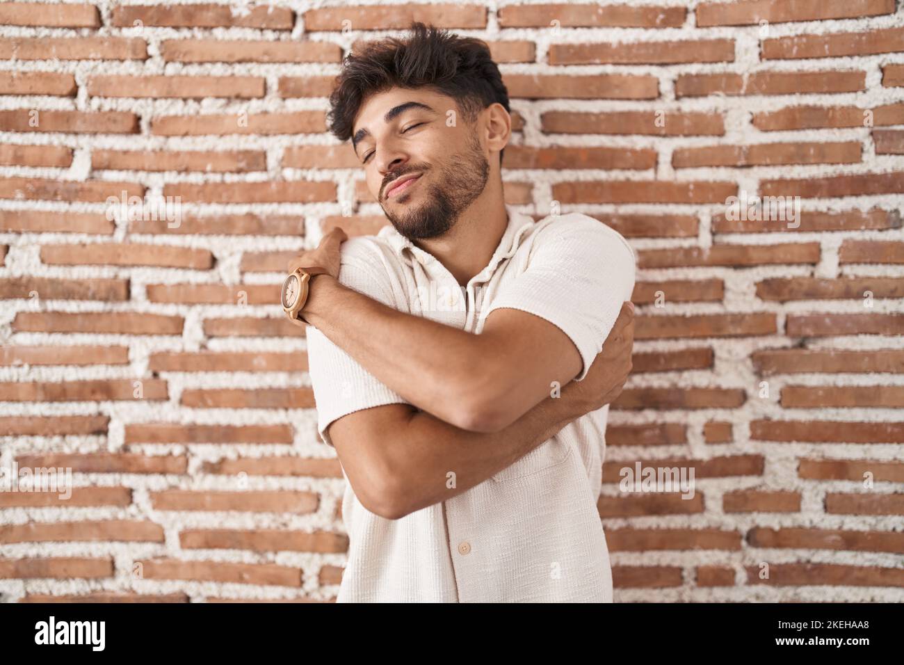 Arab man with beard standing over bricks wall background hugging ...