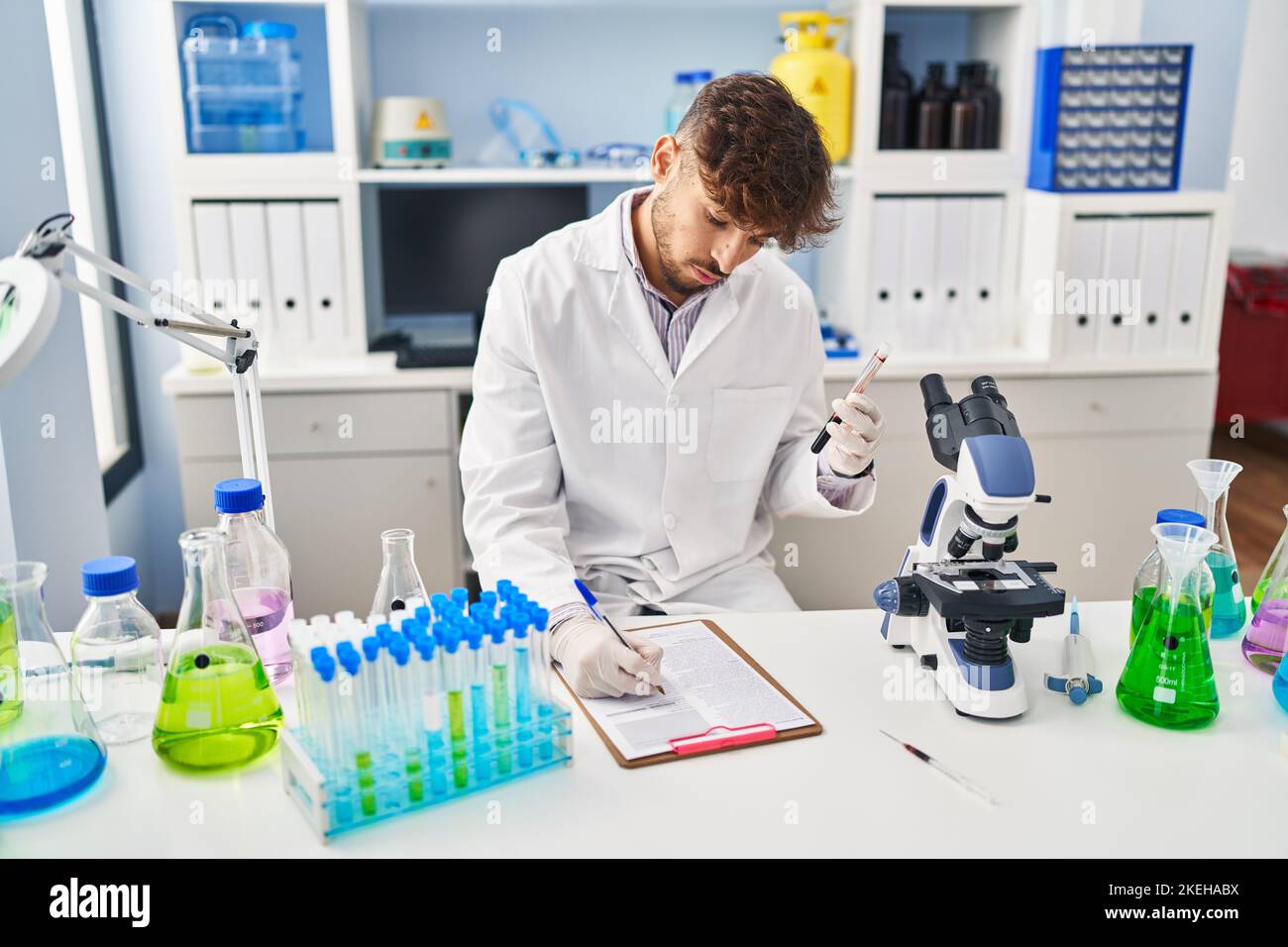 Young arab man scientist write on document analysing blood test tube at ...