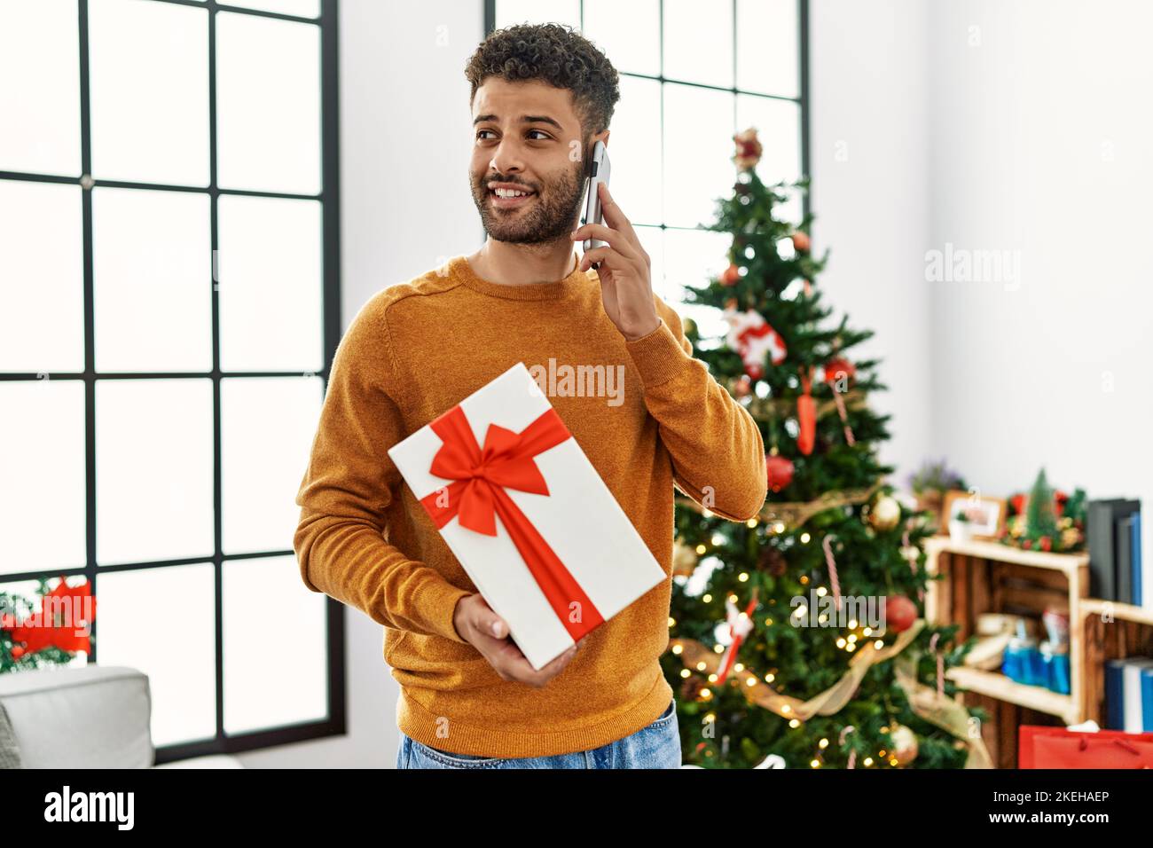Young arab man talking on the smartphone and holding gift standing by ...