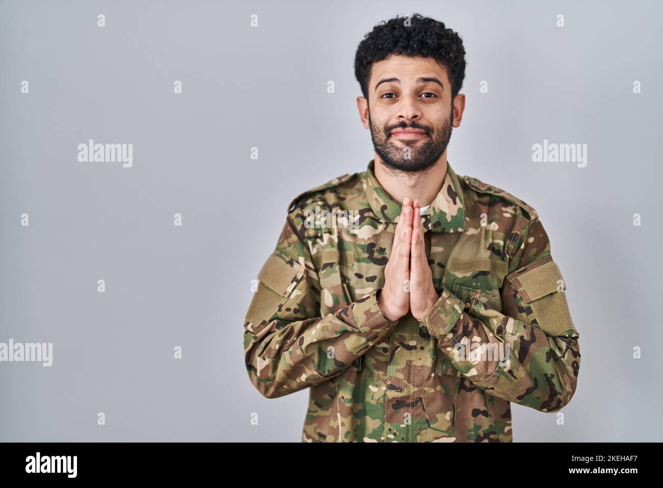 Arab man wearing camouflage army uniform praying with hands together ...