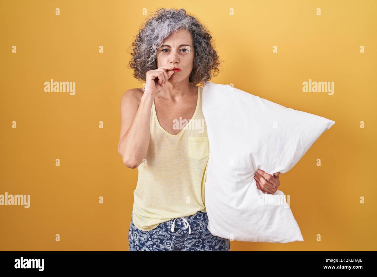 Middle age woman with grey hair wearing pijama hugging pillow mouth and ...