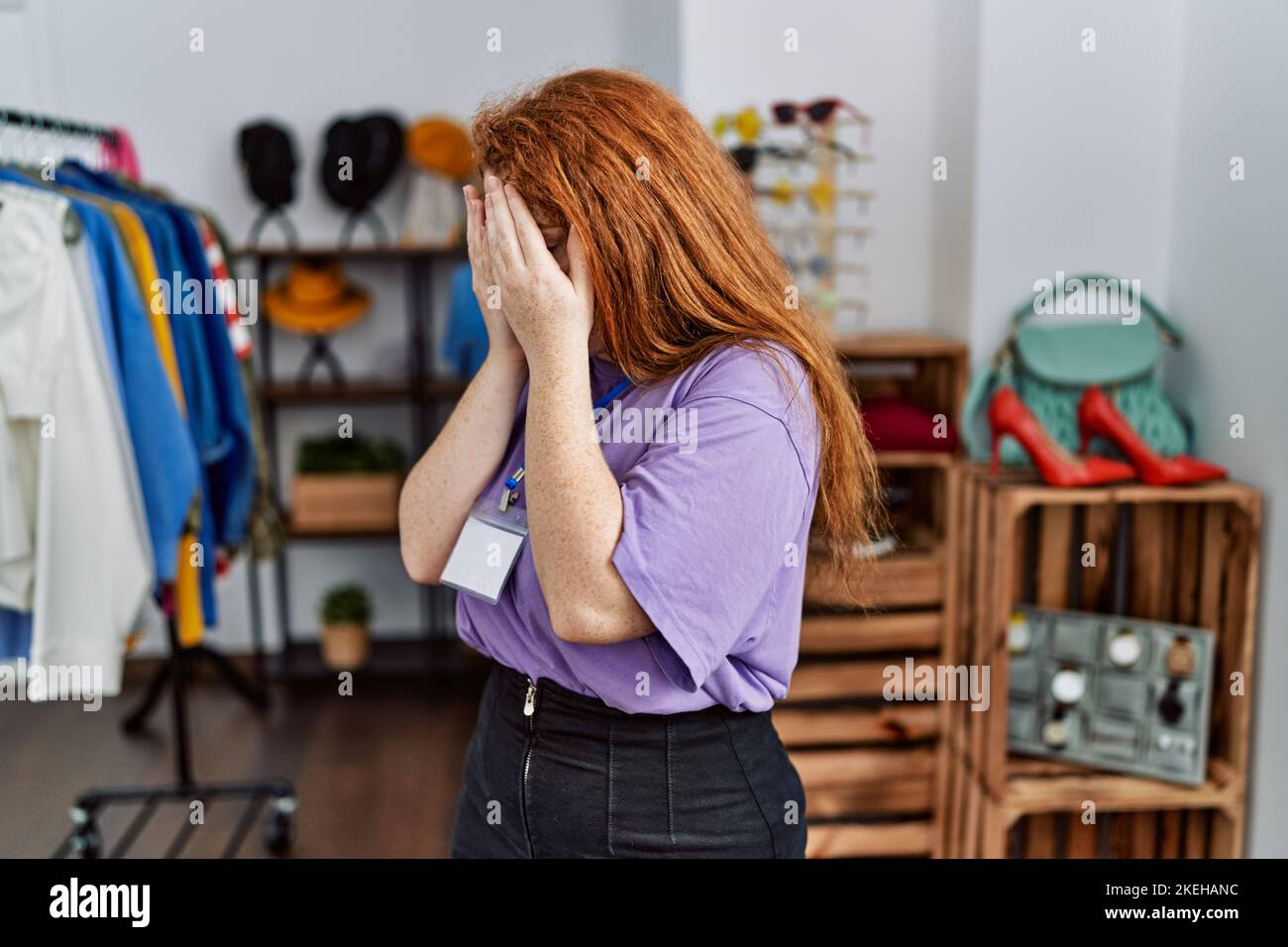 Young redhead woman working as manager at retail boutique with sad expression covering face with ...