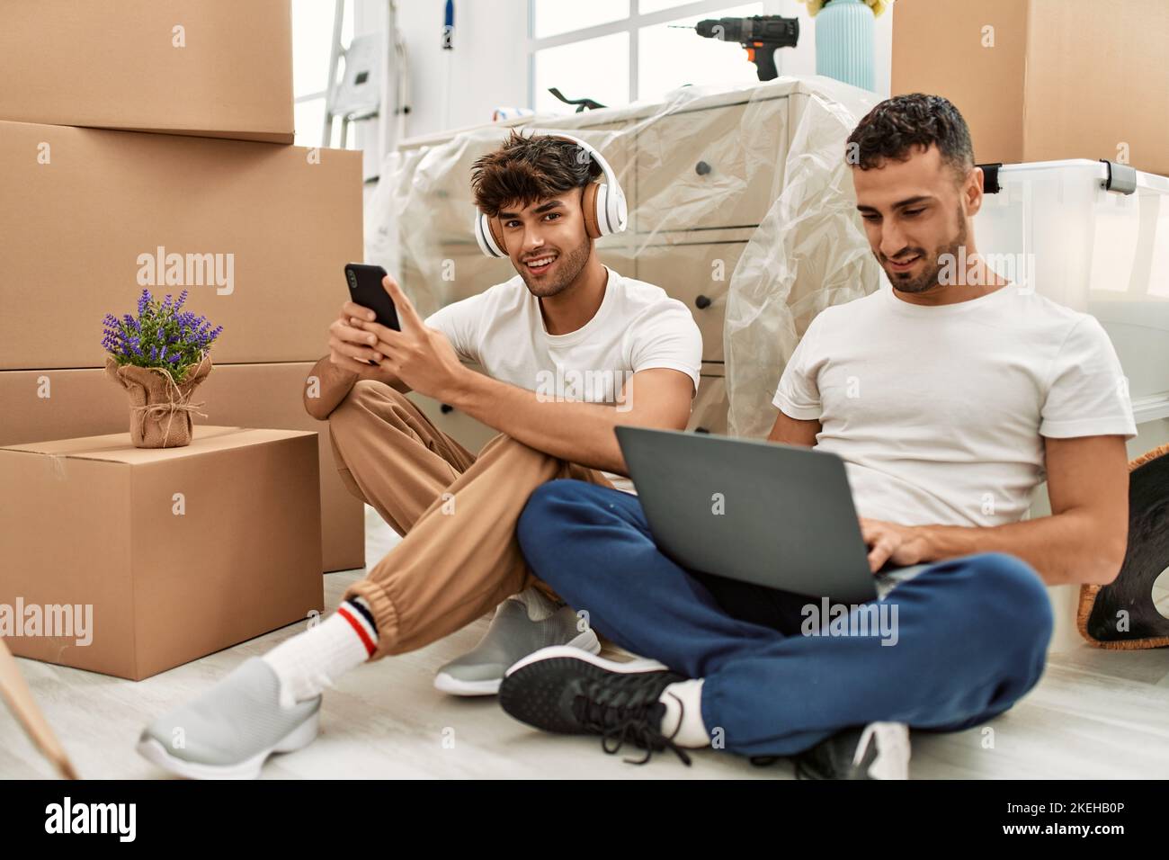 Two hispanic men couple using laptop and smartphone at new home Stock ...