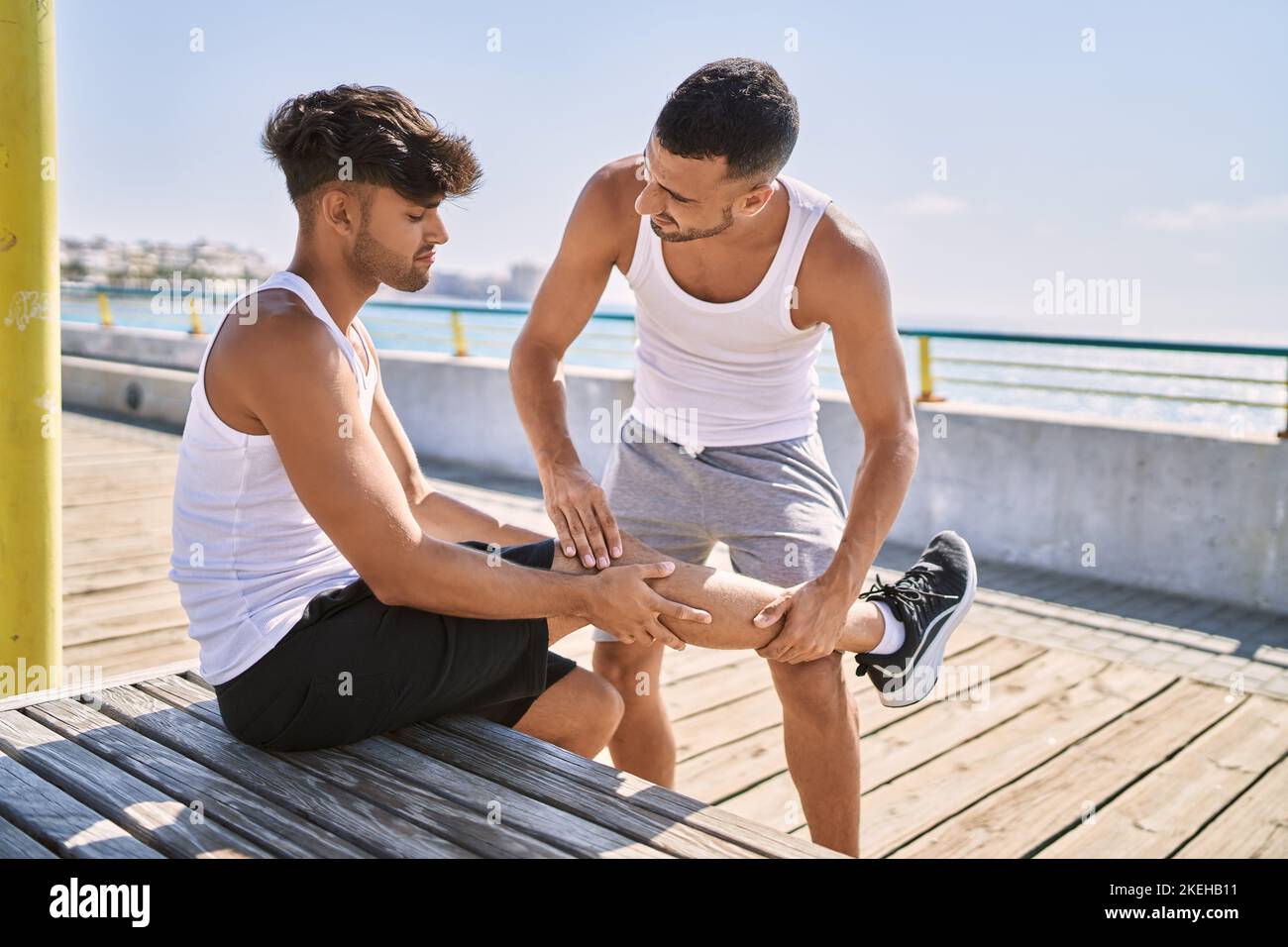 Two hispanic men sporty couple sitting on bench for leg injury at ...