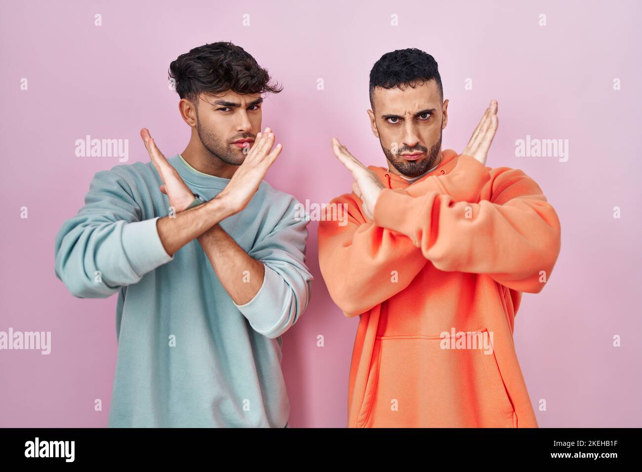 Young hispanic gay couple standing over pink background rejection ...