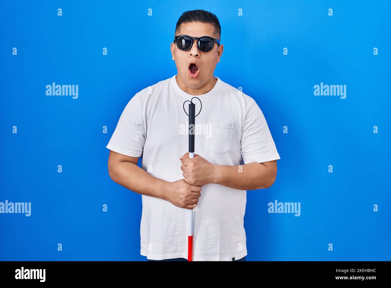 Hispanic young blind man holding cane afraid and shocked with surprise ...
