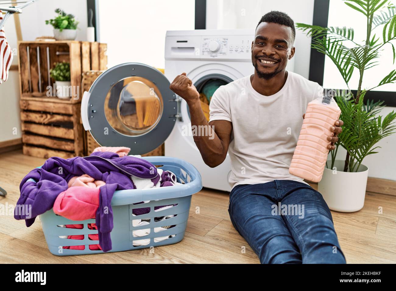 Young african man holding detergent bottle at laundry room screaming ...