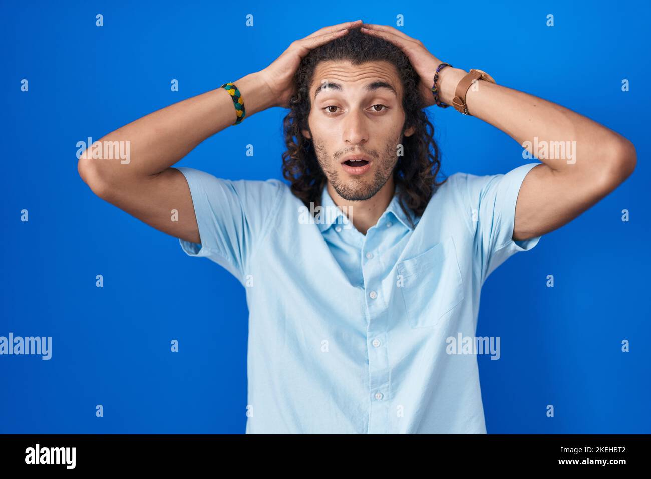 Young hispanic man standing over blue background crazy and scared with ...