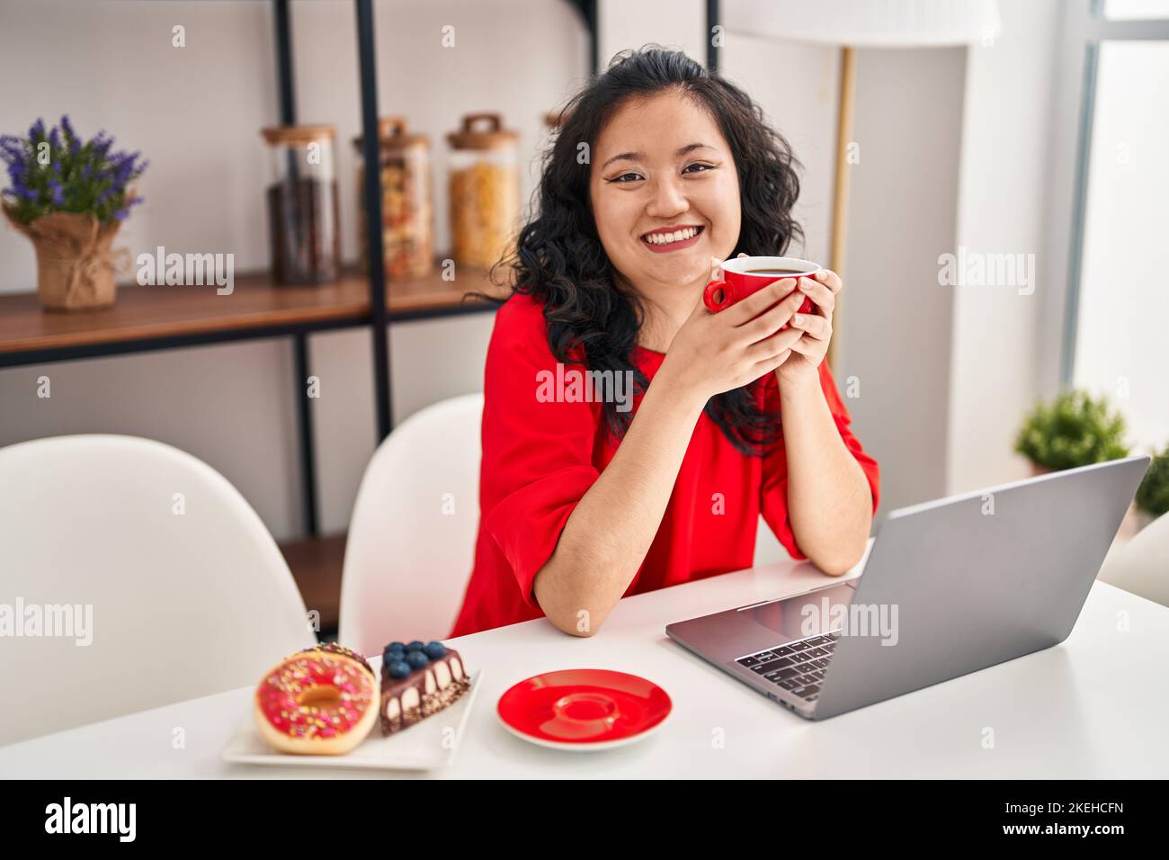 Young chinese woman having breakfast using laptop at home Stock Photo ...