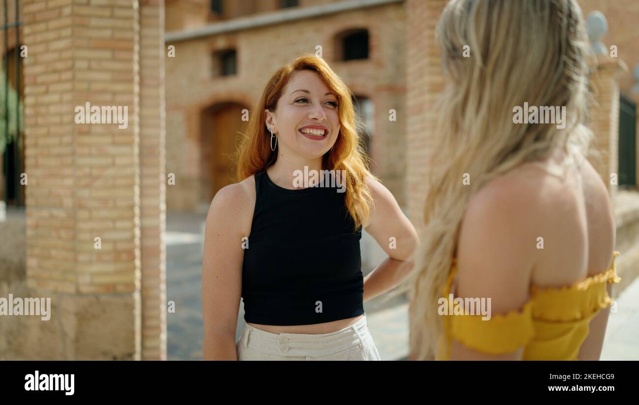 Two women standing together speaking at street Stock Photo - Alamy