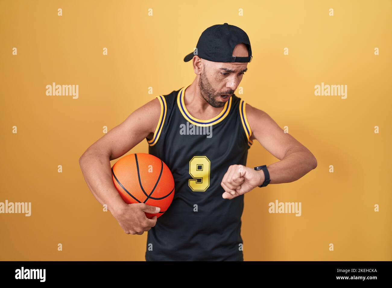 Middle age bald man holding basketball ball over yellow background ...