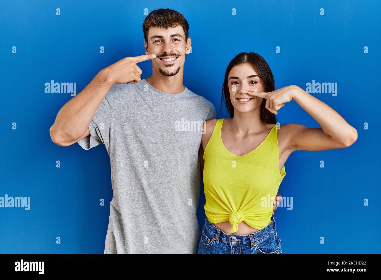 Young hispanic couple standing together over blue background pointing ...