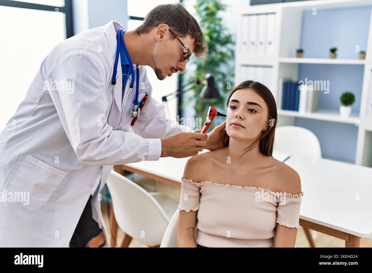 Man and woman wearing doctor uniform auscultating ear using otoscope at ...