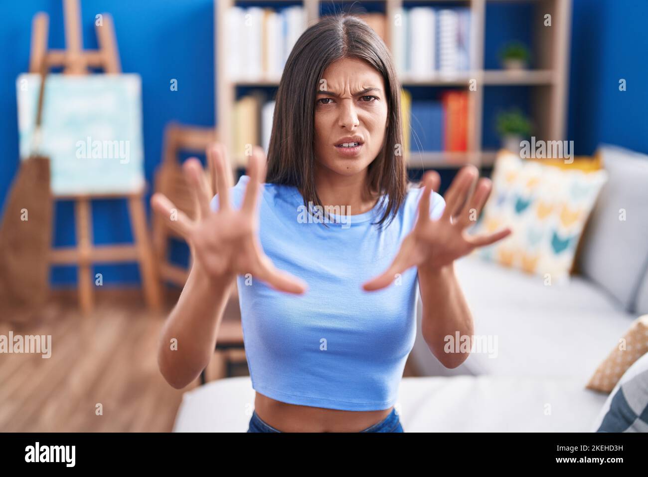 Brunette young woman sitting on the sofa at home afraid and terrified ...