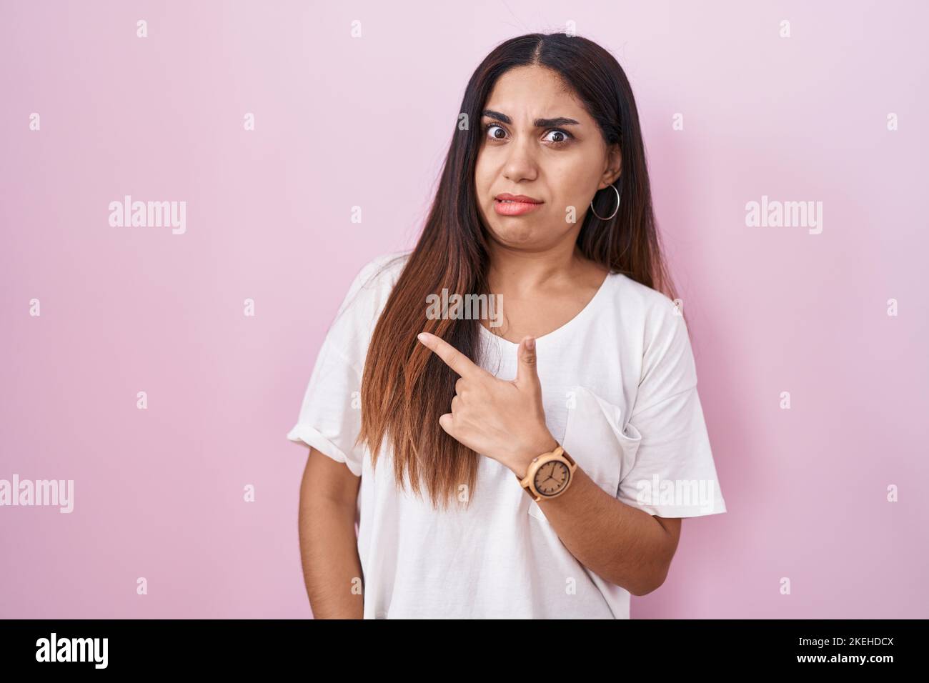 Young arab woman standing over pink background pointing aside worried ...