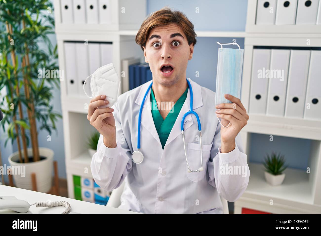 Young doctor man holding two safety mask in shock face, looking ...