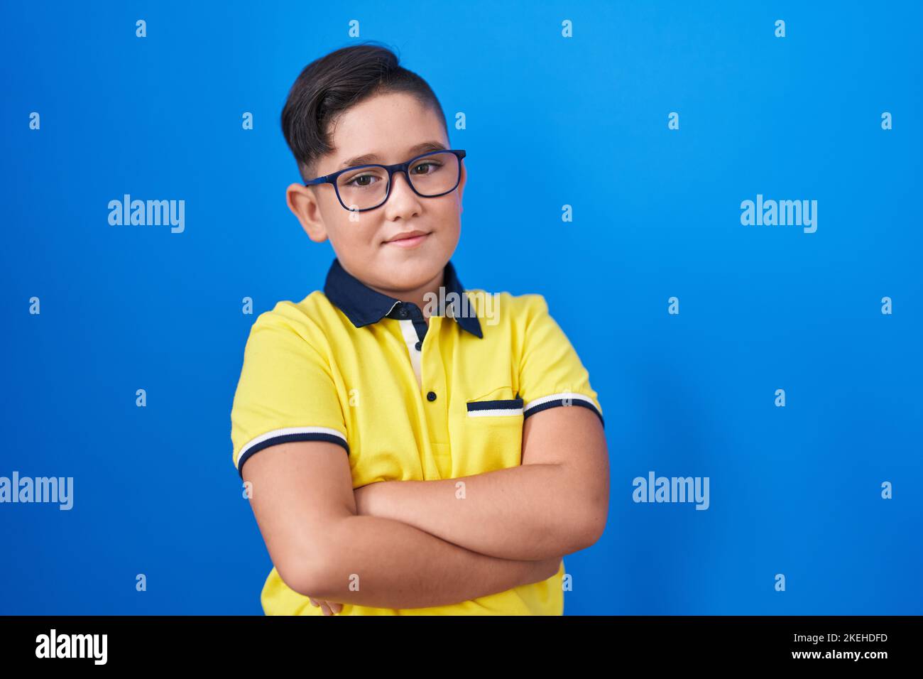 Young hispanic kid standing over blue background happy face smiling ...